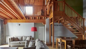 Uma sala de estar espaçosa com teto alto, escada de madeira e área de jantar.