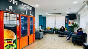 Uma área de espera moderna com assentos e uma máquina de vendas identificada como 'MINI MARKET', oferecendo comida rápida e bebidas.
