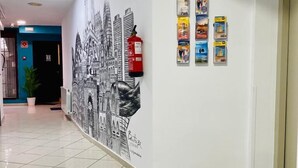 Corredor com um grande mural de uma paisagem urbana, um extintor de incêndio e vários folhetos de viagem na parede.
