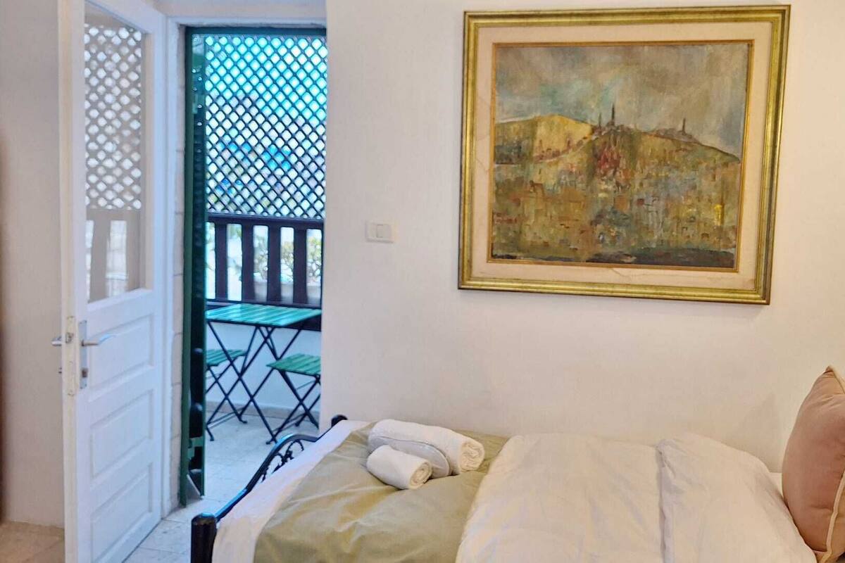 Quarto com cama, um quadro na parede e vista para uma varanda com porta treliçada.
