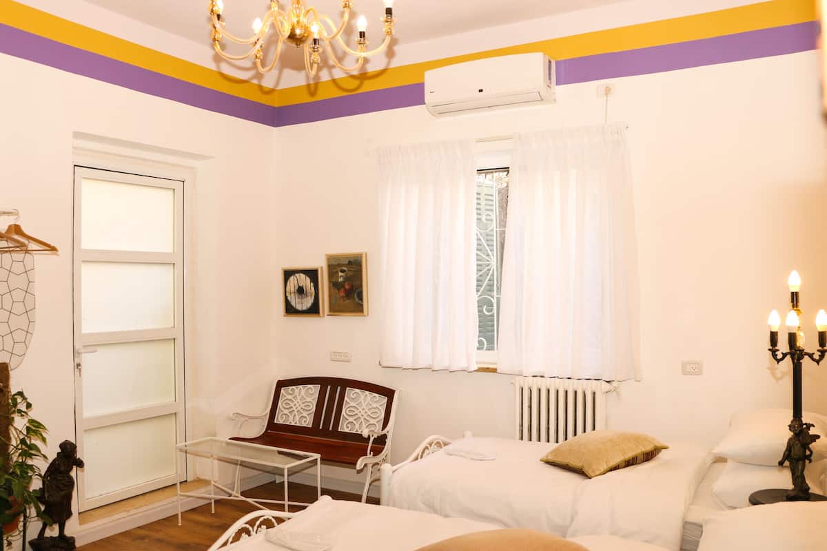 Quarto com cama, mesa de cabeceira, cadeira, janela com cortinas e um lustre.