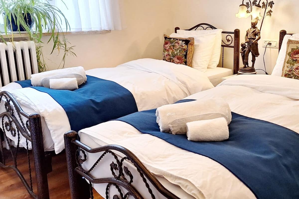 Quarto duplo com duas camas, cada uma com colcha azul e branca, almofadas brancas e uma pequena estatueta na cabeceira.