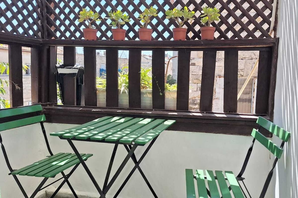 Uma varanda com mesa e cadeiras verdes, um painel treliçado e plantas em vasos.