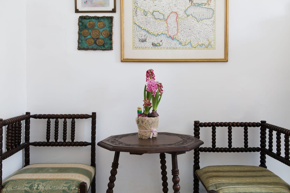 Quarto com duas cadeiras de madeira, uma mesinha redonda e um mapa fixado na parede.