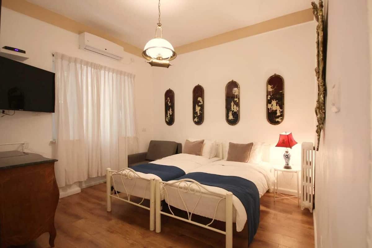 Quarto com cama de casal, escrivaninha, cadeira, televisão e radiador.