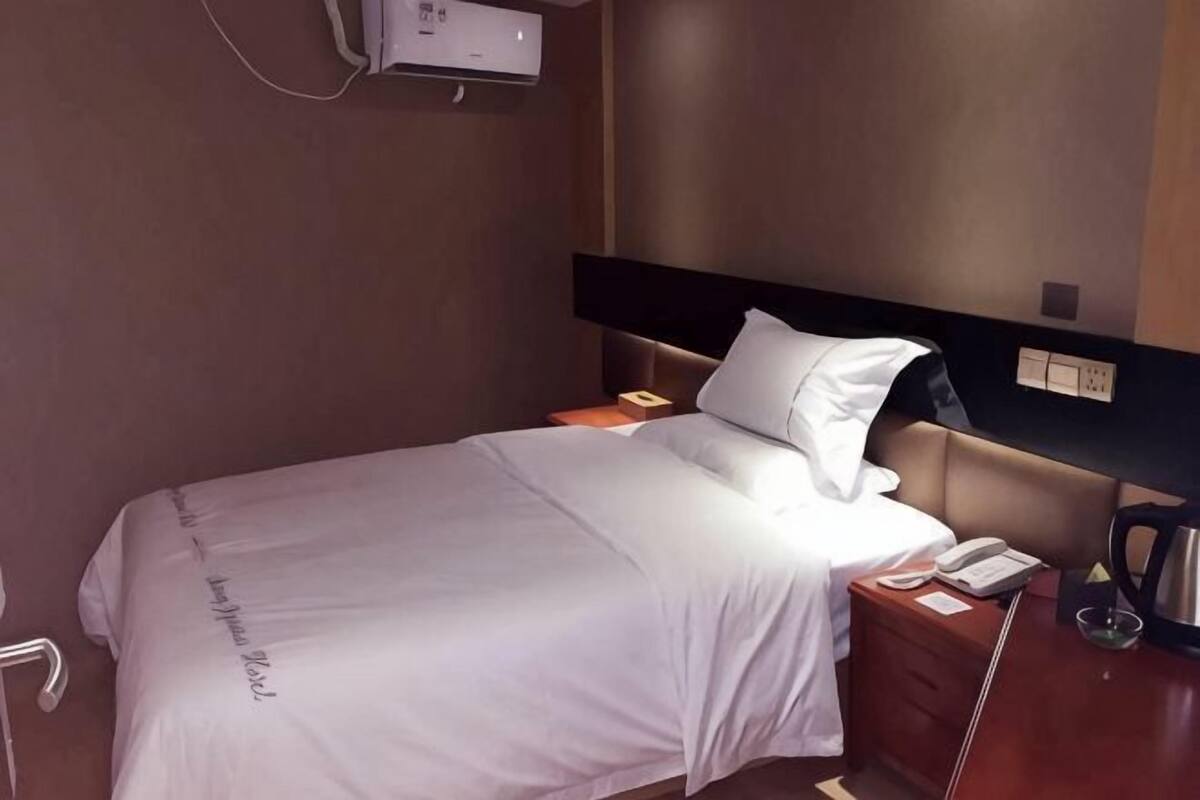 Quarto de hotel com cama, mesa de cabeceira, luminária e ar-condicionado fixado na parede.