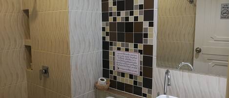 Casa de banho com chuveiro, sanita, lavatório e parede em mosaico.