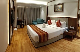 Quarto de hotel com uma cama grande, uma escrivaninha, uma cadeira, uma TV e um quadro na parede.