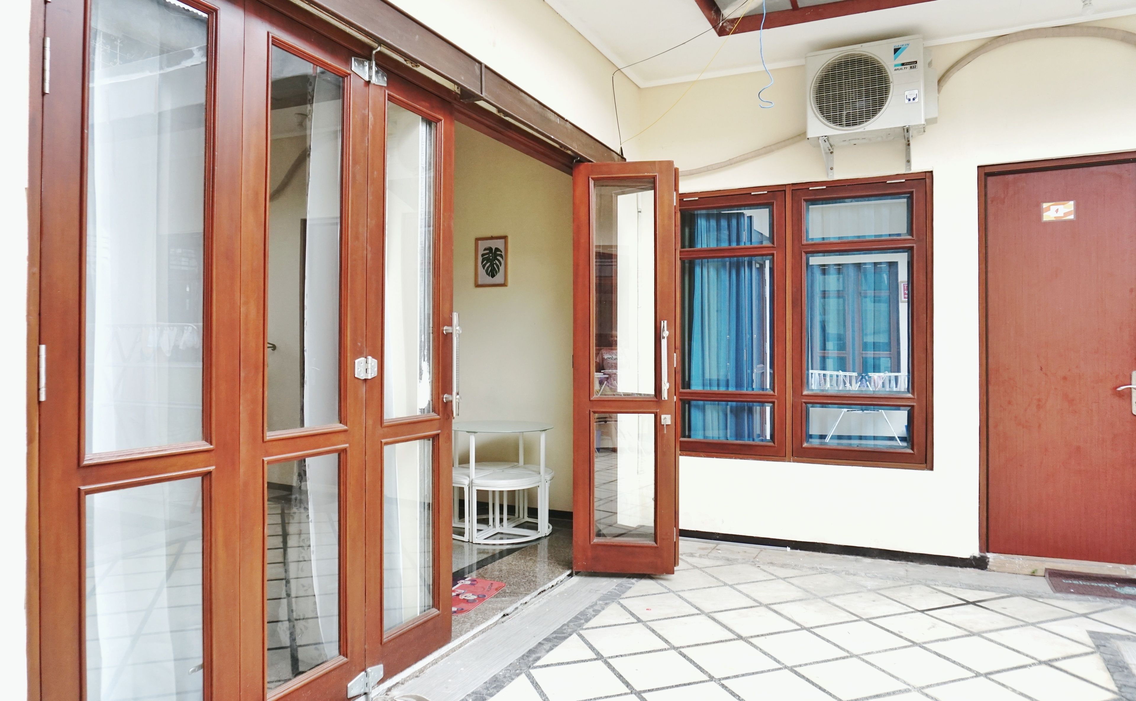 Um quarto com soalho em mosaico, porta de madeira e janela com cortinas.