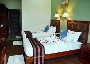 Quarto de hotel com duas camas, cabeceiras de madeira, uma escrivaninha de madeira e duas luminárias fixadas na parede.