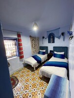 Quarto com duas camas individuais, piso estampado, janela com cortinas e luminária pendente.