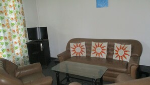 Uma sala de estar com um sofá marrom, duas poltronas, uma mesa de centro de vidro e uma TV de tela plana em um suporte.