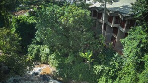 Um edifício de vários andares com arquitetura tradicional, rodeado por vegetação exuberante e um rio sinuoso.