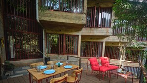 Um deck de madeira com mesa e cadeiras, cercado por grades vermelhas e vasos de plantas.