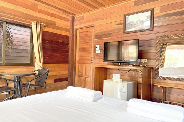 Quarto de cabana de madeira com cama, televisão, mesa pequena e janela.