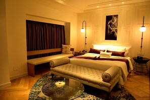 Quarto de hotel com cama, sofá, um banco, uma mesa pequena e duas luminárias.
