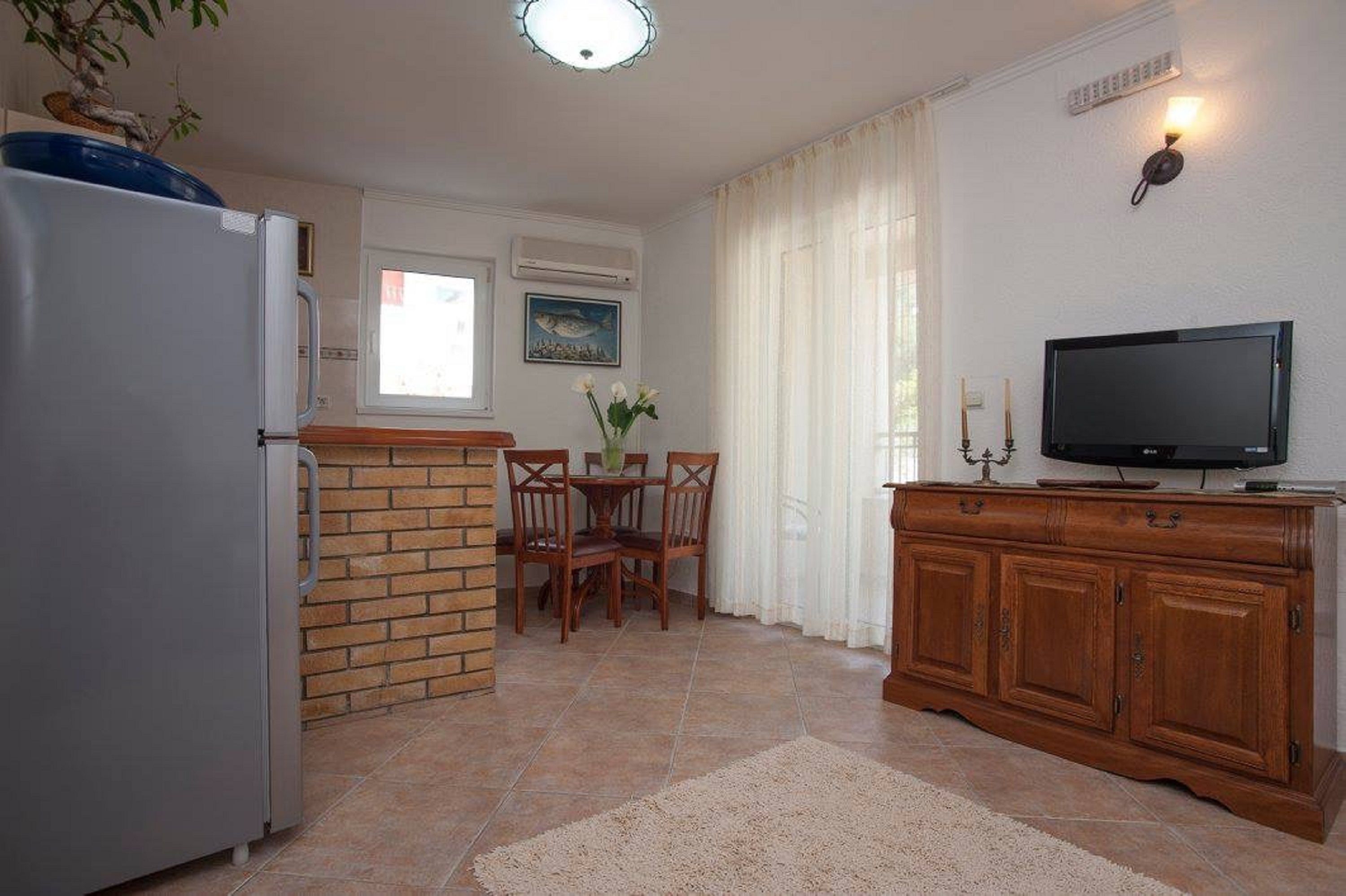 Uma cozinha compacta com geladeira, divisória de tijolos, mesa de jantar com cadeiras, televisão em um armário de madeira e janela com cortinas.