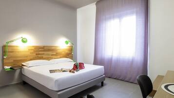 Quarto de hotel com cama, luminárias de cabeceira, escrivaninha e uma cadeira.