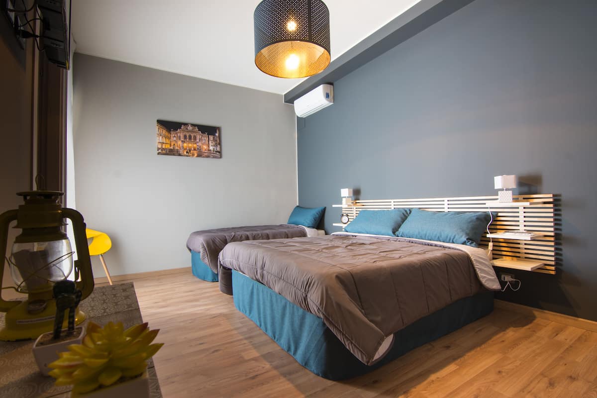 Quarto com duas camas, uma mesa de cabeceira, uma luminária e ar condicionado fixado na parede.