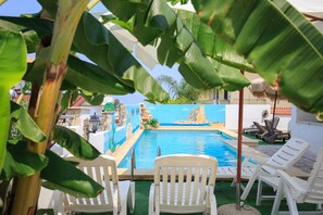 Área de piscina com cadeiras de lounge brancas e um mural de uma paisagem praiana.