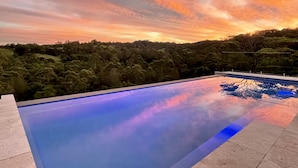 Piscina infinita com vista desimpedida do pôr do sol sobre uma paisagem arborizada.