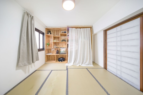 Um quarto japonês tradicional com tatames, uma estante de madeira com diversos objetos e uma porta deslizante.