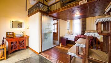 Um quarto tradicional japonês, com piso de tatame, porta deslizante, cama de madeira com manta vermelha e uma pequena mesa com cadeira de fibra natural.