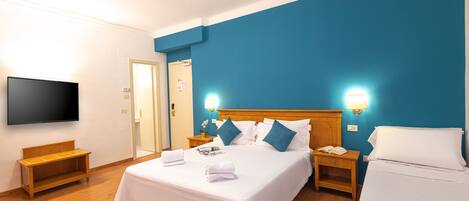 Quarto de hotel com uma cama grande, mesas de cabeceira, televisão de tela plana e um banco de madeira.