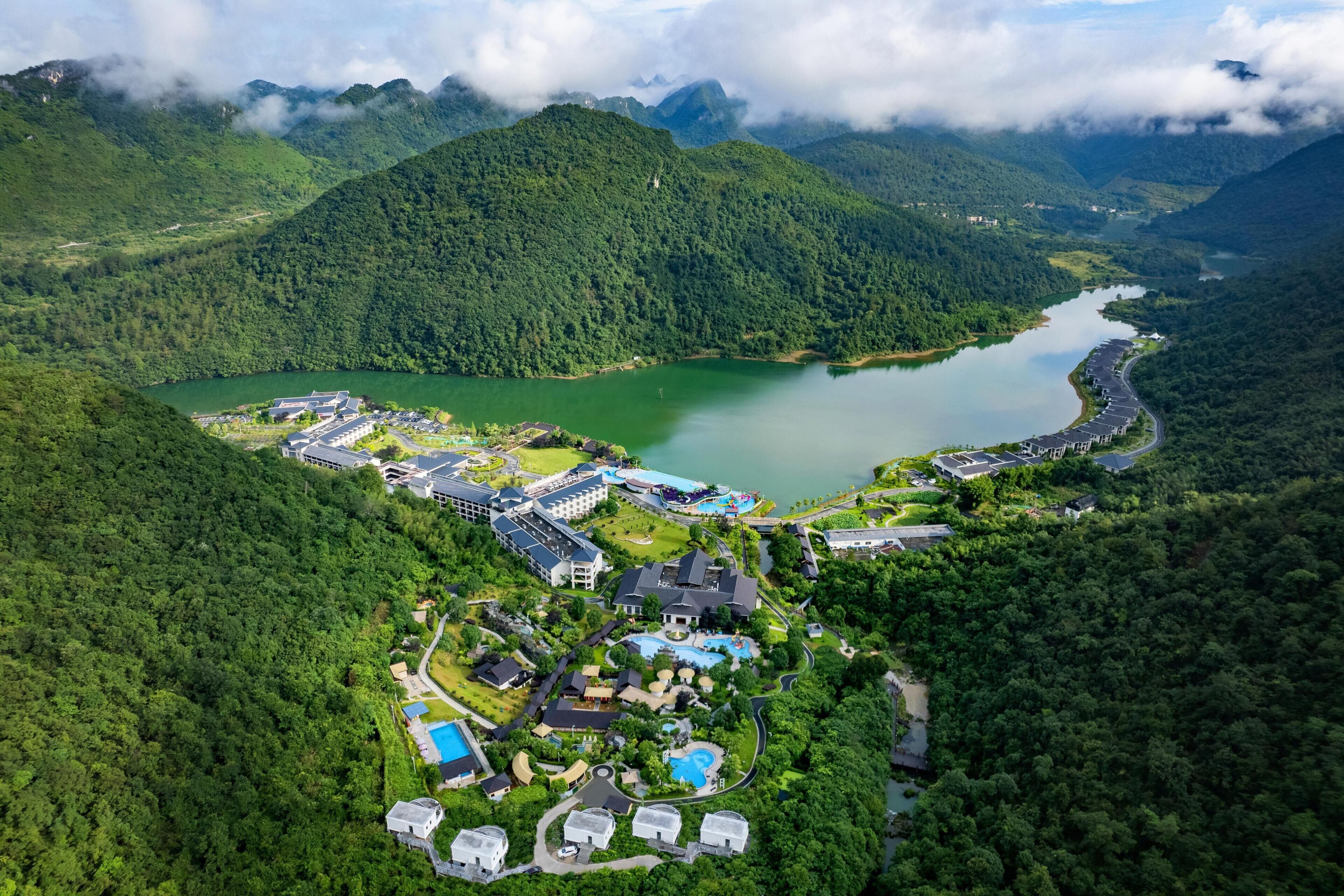 Um resort com vários edifícios, piscina e um lago rodeado por colinas arborizadas.