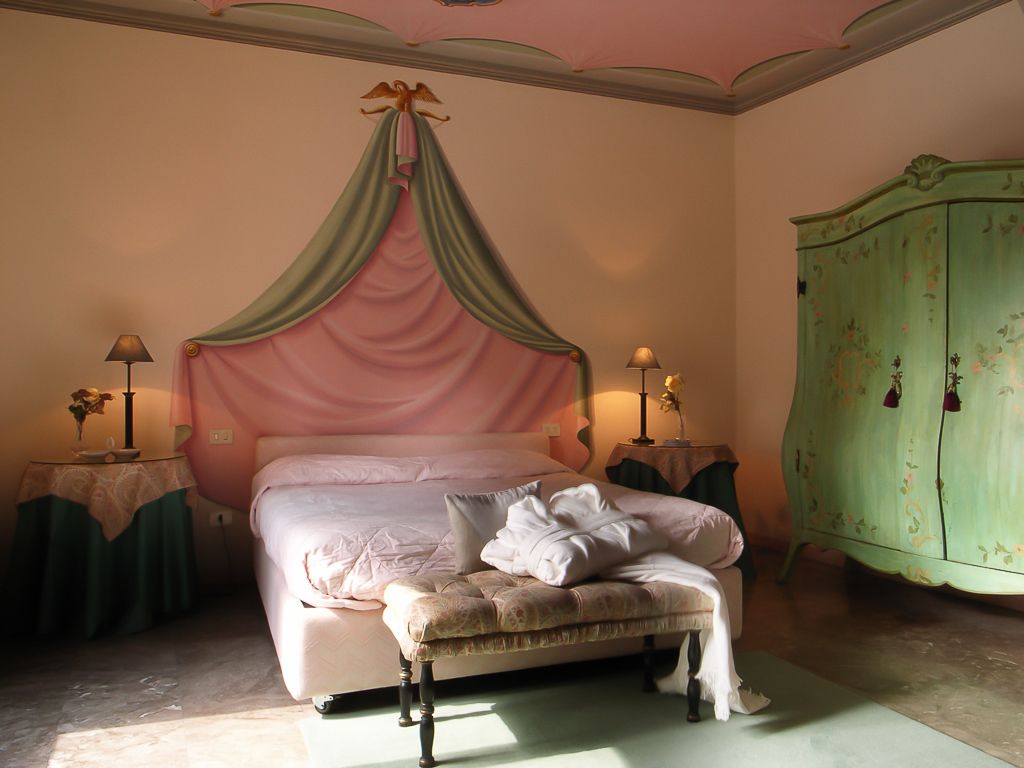 Quarto com cama de dossel, um guarda-roupa verde e duas mesas de cabeceira com abajures.