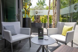 Área externa moderna com assentos, duas poltronas cinzas estofadas e uma mesa redonda pequena, com um código QR para aplicativo móvel.