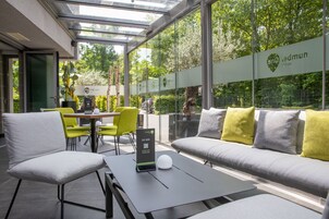 Uma área externa moderna com assentos fechada por vidro, um sofá com almofadas e uma mesa com um sinal de código QR.