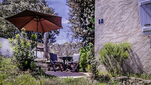 Um terraço ao ar livre com mesa, cadeiras, um grande guarda-sol e um muro de pedra.