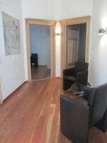 Uma sala de estar com piso de madeira, um sofá preto, uma mesa de centro de vidro e um quadro na parede.