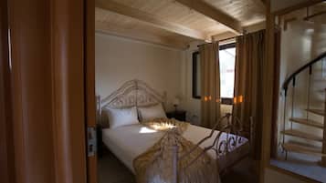 Quarto com teto de madeira, cama com cabeceira decorativa, mesa de cabeceira e escada à direita.