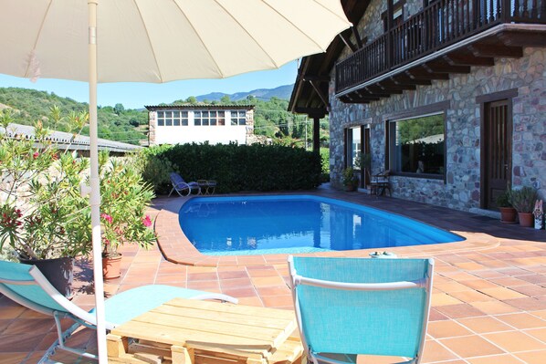 Piscina com deck de madeira, espreguiçadeiras e um grande guarda-sol.
