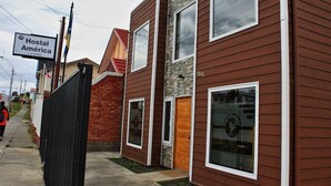 Uma fileira de casas de madeira marrom com molduras de janela brancas e uma placa com a inscrição 'Hostal América'.