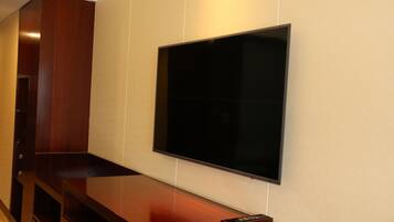 Uma sala de estar moderna com uma TV de tela plana fixada na parede, um centro de entretenimento de madeira e um controle remoto no console central.