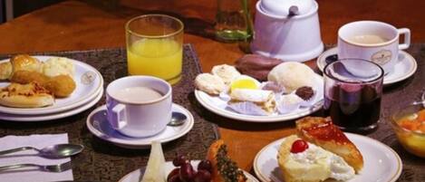 Uma mesa posta para o café da manhã, com diversos pratos, incluindo doces, frutas e bebidas.