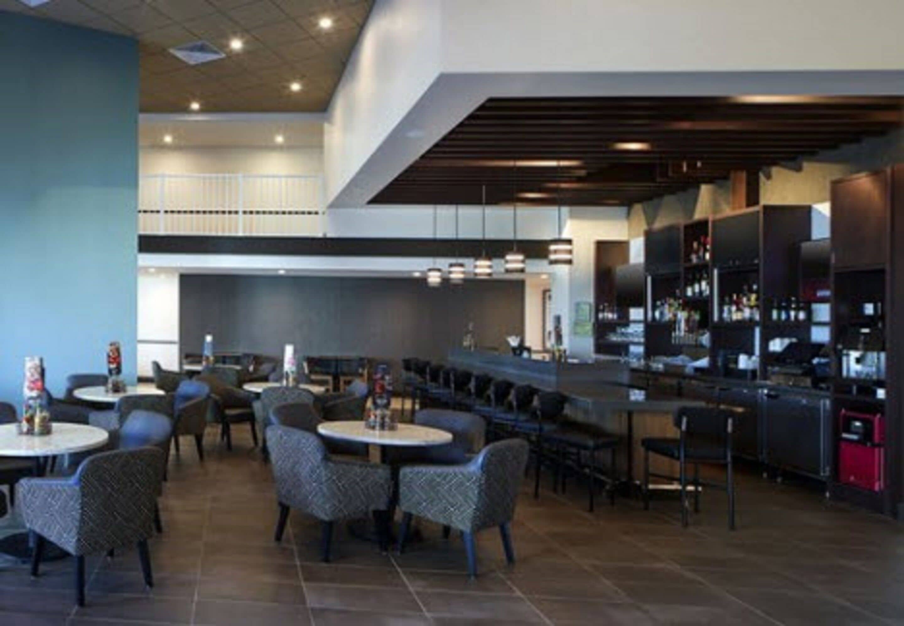 Um restaurante moderno com mesas e cadeiras redondas, um espaço de bar e uma cozinha ao fundo.