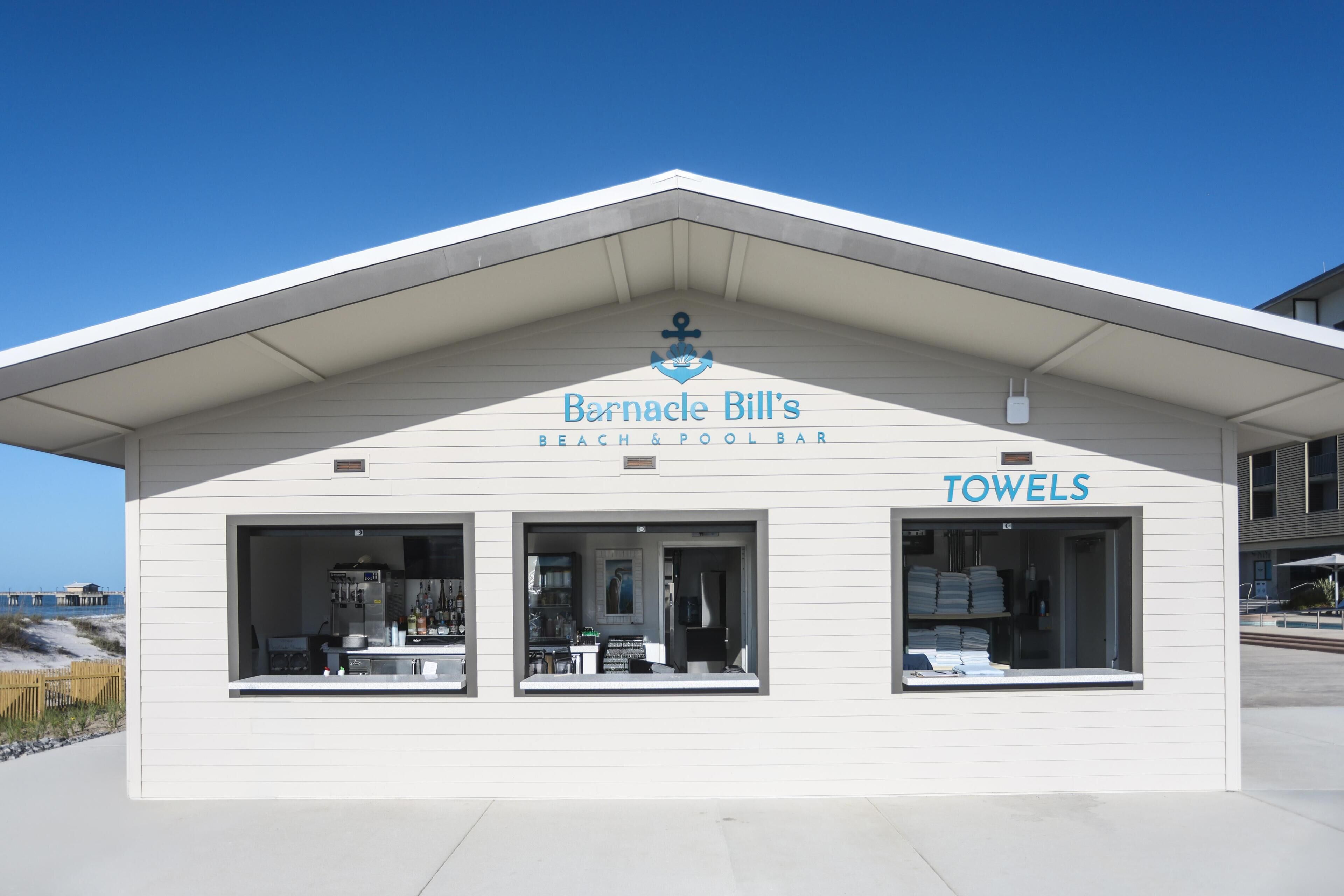 Um bar de praia com um letreiro que diz 'Barnacle Bill's Beach & Pool Bar' e uma janela com a inscrição 'TOWELS'.