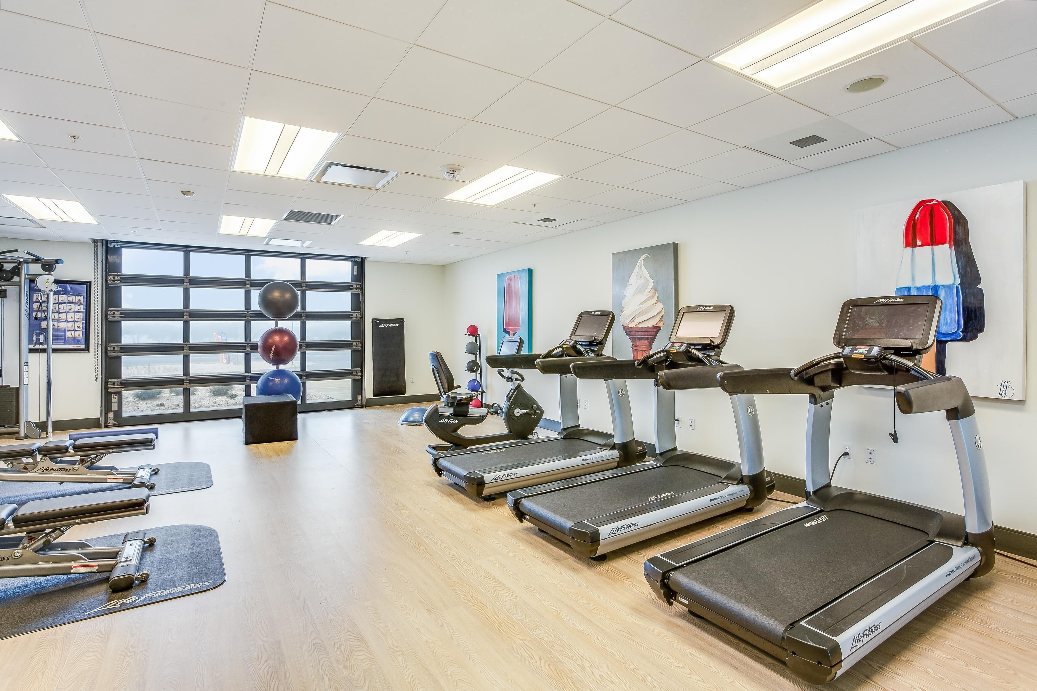 Uma academia com esteiras, bolas de exercício e um remo.