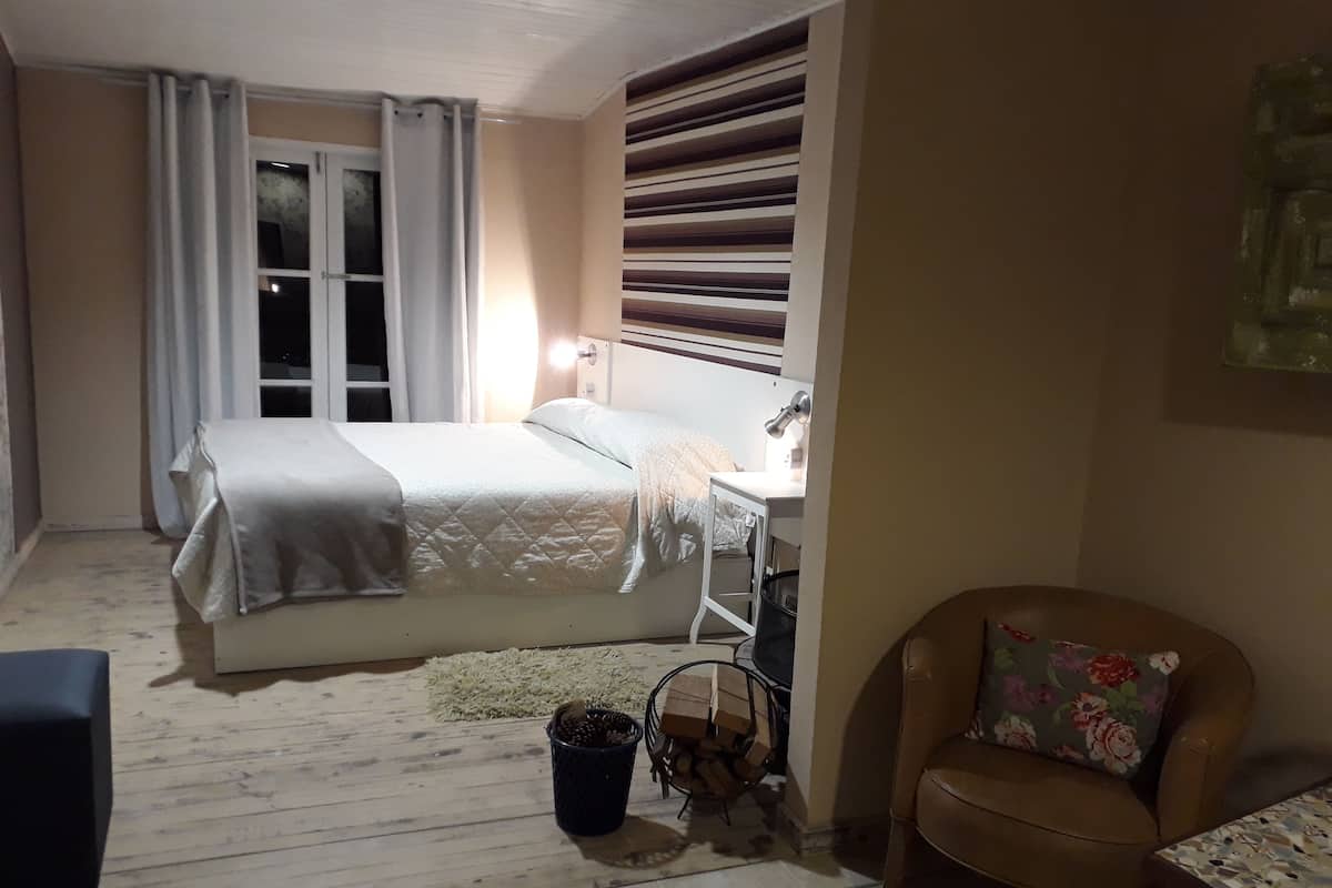 Um quarto com cama, mesa de cabeceira, abajur, cadeira e uma mesinha.