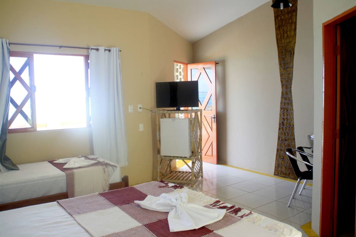 Quarto com duas camas, televisão sobre suporte, uma cadeira e janela com cortinas.