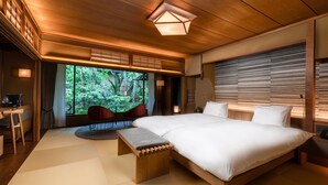 Quarto moderno com cama grande, detalhes em madeira, vista para área verde e escrivaninha com cadeira.