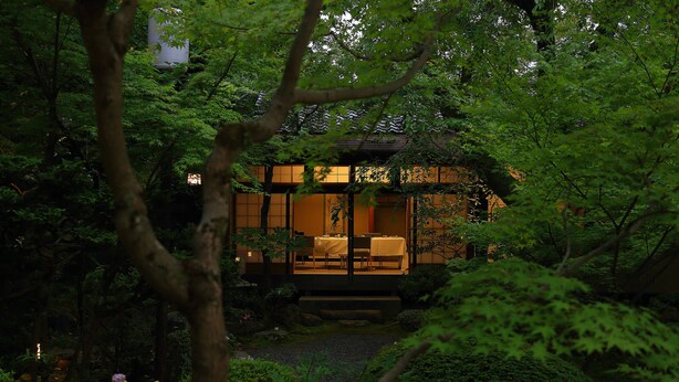 Um edifício tradicional japonês com tatames, varanda de madeira e vista para um jardim exuberante.