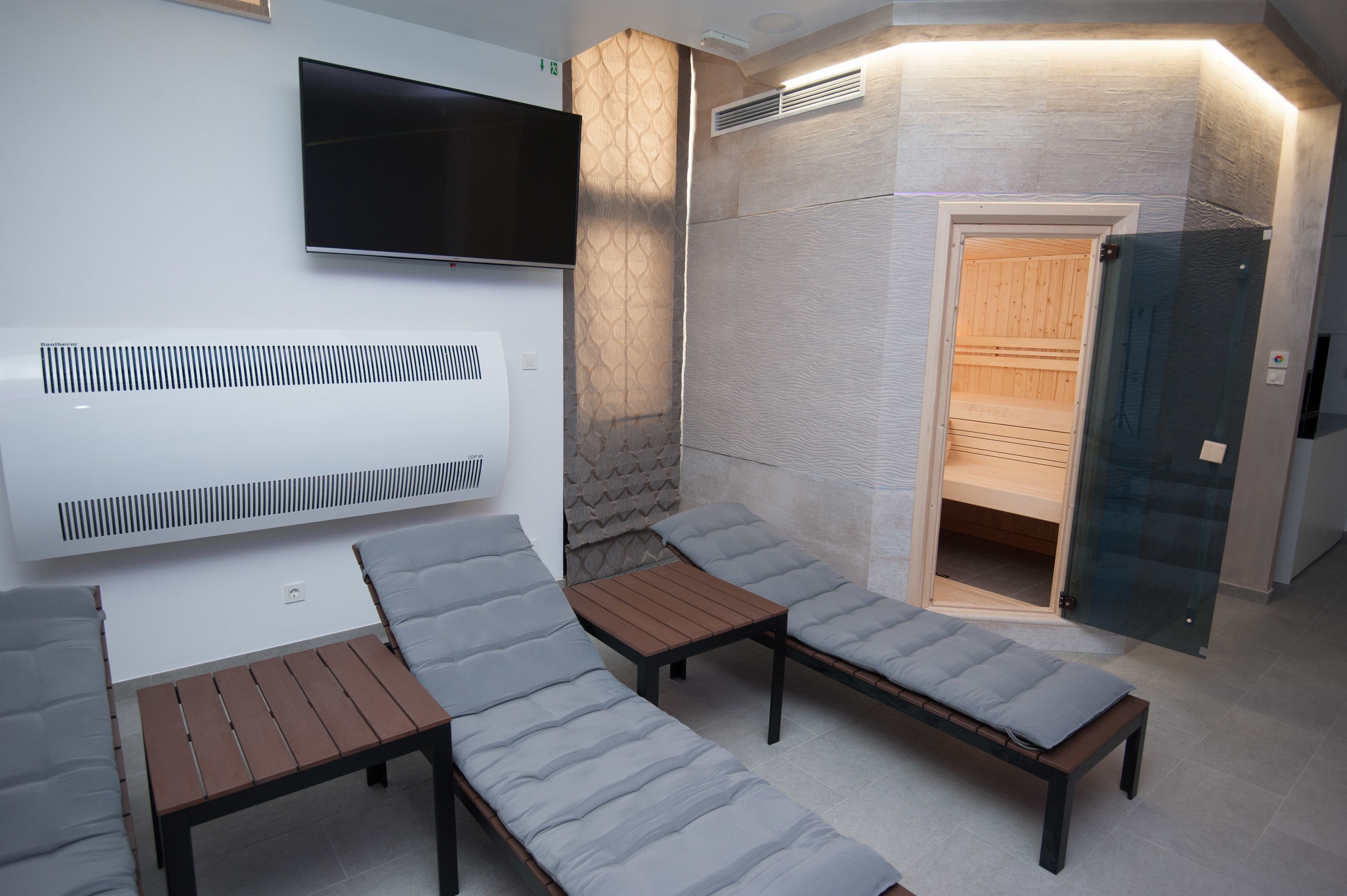 Quarto moderno e bem iluminado, com televisão de tela plana na parede, aquecedor embutido e porta de madeira para a área do chuveiro.