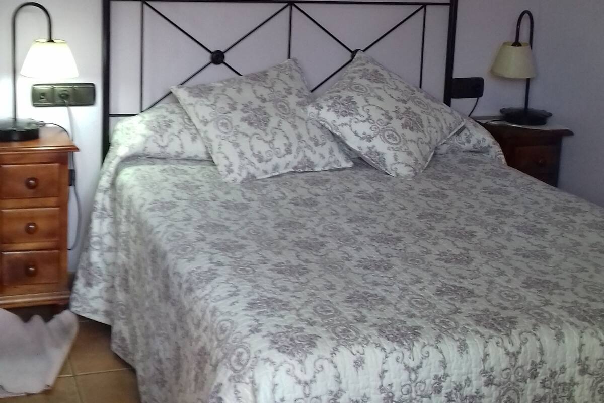 Quarto com cama, mesa de cabeceira, abajur e quadro na parede.