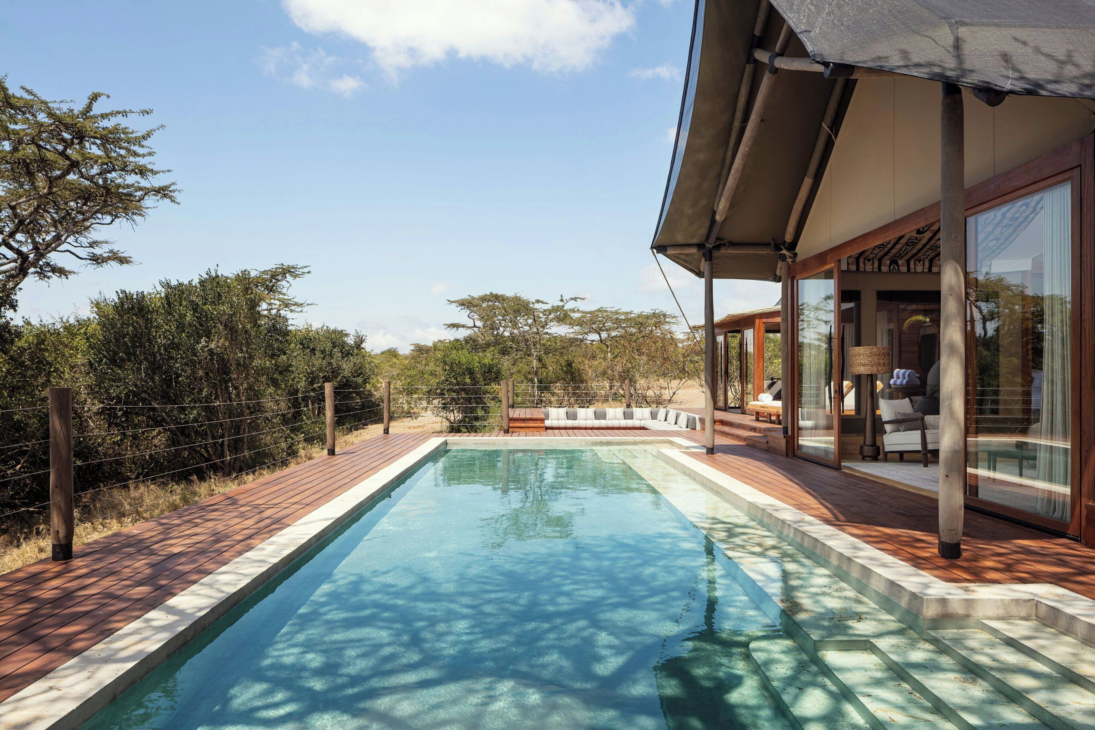 Uma piscina com deck de madeira, área de estar coberta e vista para a paisagem ao redor.