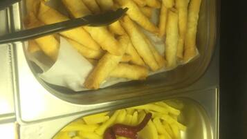 Uma bandeja com rolinhos primavera dourados e caseiros e um recipiente com batatas fritas, acompanhado de um garfo de plástico.